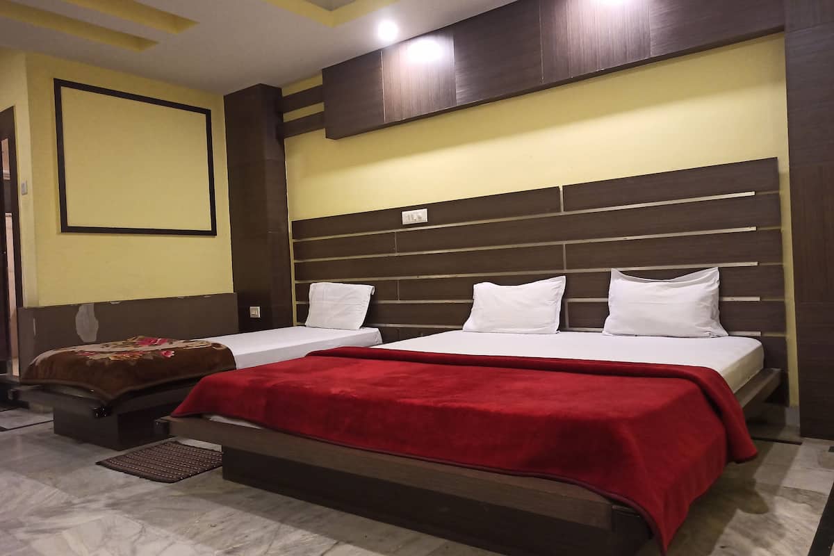 Quarto de hotel com duas camas, um cobertor vermelho na cama maior e um banco marrom.