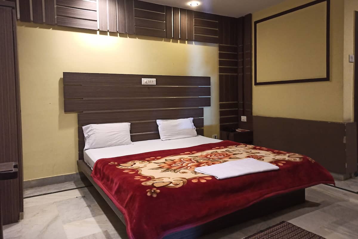 Quarto de hotel com cama, mesa de cabeceira, telefone fixado na parede e porta.