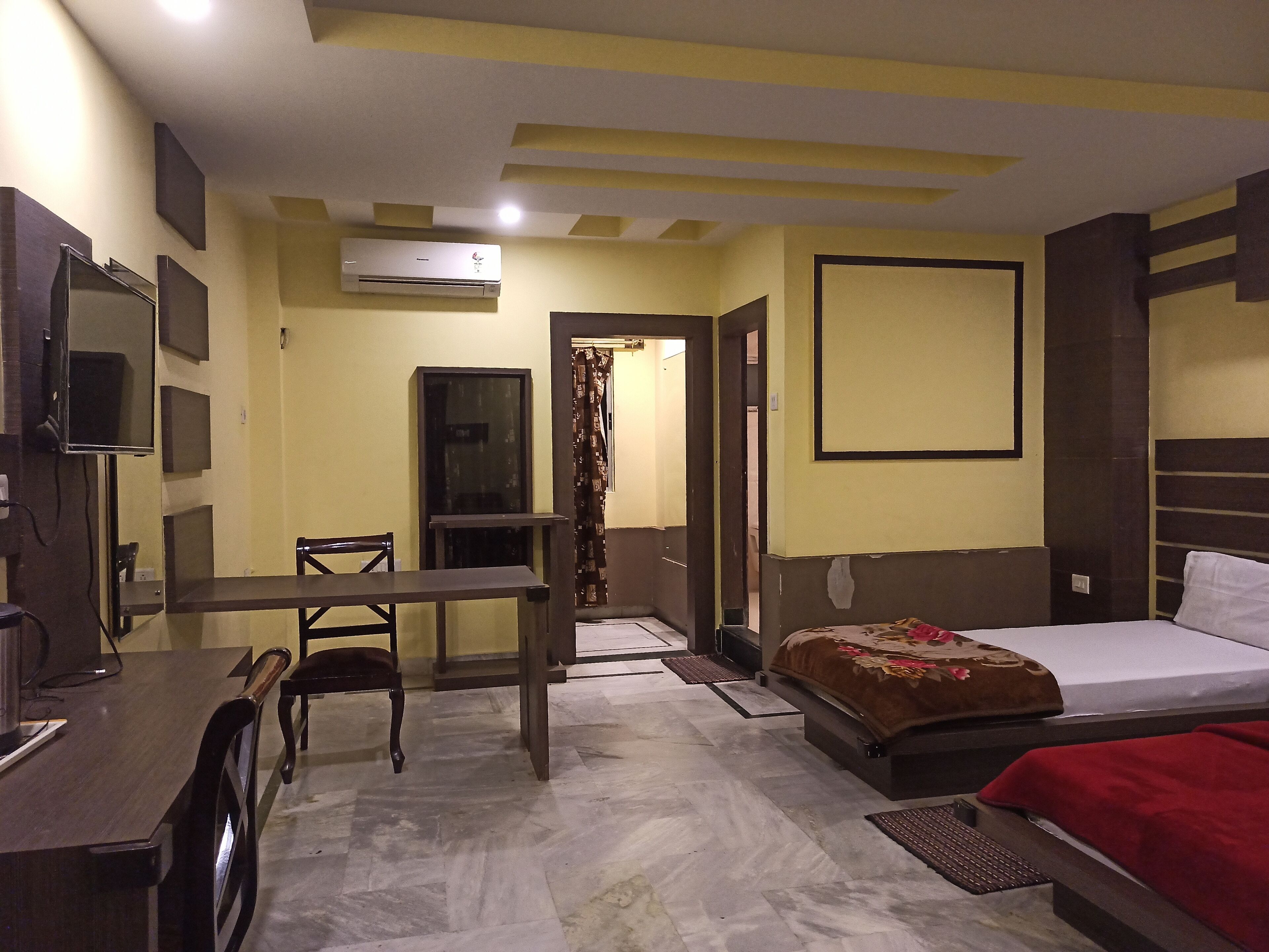 Quarto de hotel com cama, escrivaninha, cadeira, televisão e ar condicionado.