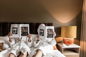 Quarto de hotel com uma cama, uma mesa de cabeceira com luminária e uma revista.