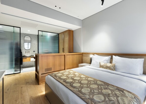 Quarto de hotel moderno com uma cama grande, um guarda-roupa de madeira, cabine de chuveiro em vidro e um banheiro com um espelho amplo e pia.