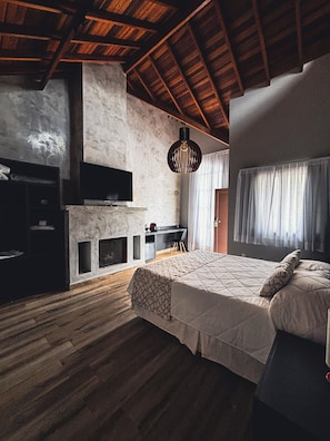 Quarto com uma cama grande, uma escrivaninha, uma televisão e uma lareira.