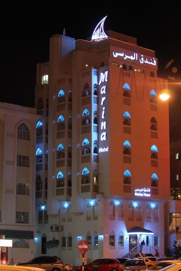 Um hotel com vários andares, sinalização iluminada, um letreiro grande no terraço e entrada visível.