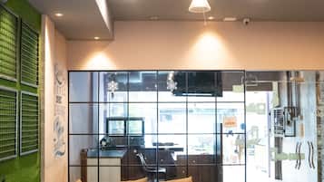 Um interior moderno com área de estar, divisória de vidro e uma cafeteria visível ao fundo.