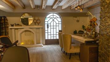 Um quarto acolhedor com lareira, vigas de madeira, parede de pedra e um espaço de refeições com cadeiras e mesa.