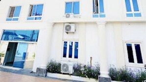 Um hotel com vários andares, fachada branca, várias janelas e aparelhos de ar condicionado.