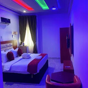 Quarto de hotel com cama, mesa de cabeceira, luminária e televisão na parede.