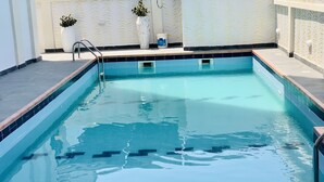 Uma piscina interior retangular com água azul cristalina, bordas azulejadas e uma cadeira de banho vermelha em primeiro plano.