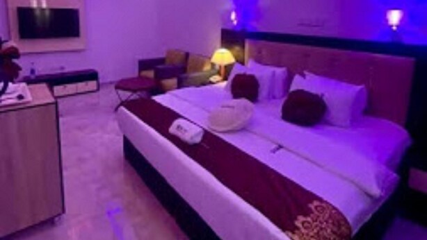 Quarto de hotel moderno com uma cama grande, mesas de cabeceira, escrivaninha e televisão.