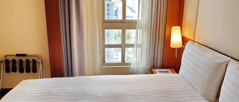 Quarto de hotel com cama grande, janela com cortinas, abajur e radiador fixado na parede.