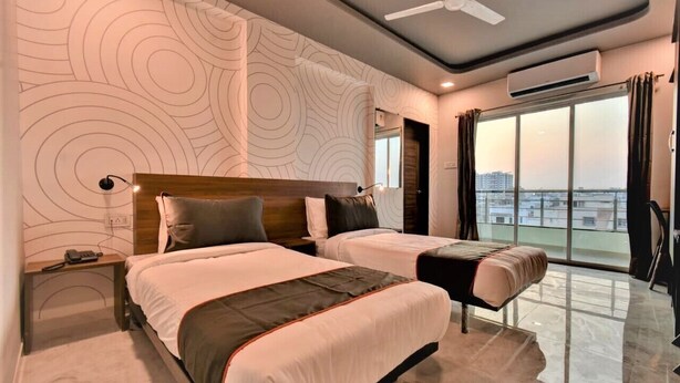 Quarto de hotel moderno com duas camas, ventoinha no teto, ar condicionado e uma ampla janela com vista para a cidade.