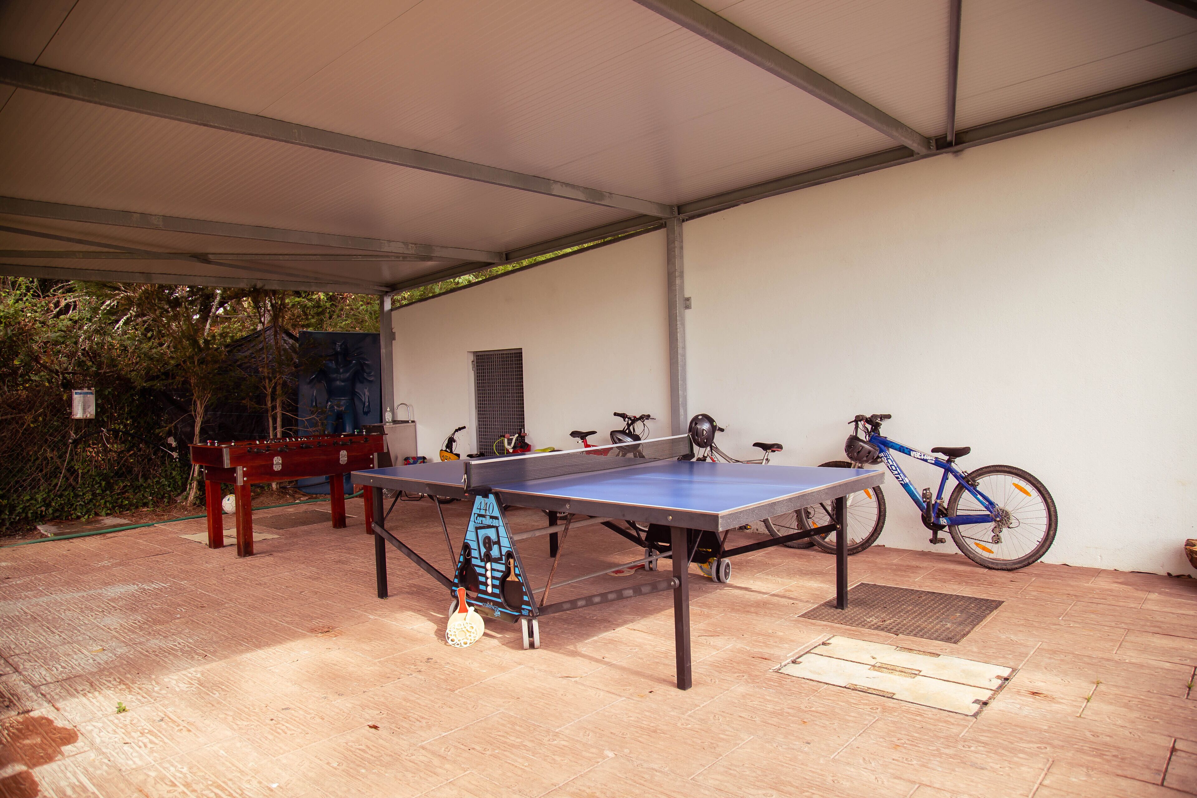 Uma área externa coberta com mesa de pingue-pongue, bicicleta e mesa de tênis.