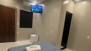 Quarto de hotel com uma cama, televisão na parede, ar condicionado e uma porta.