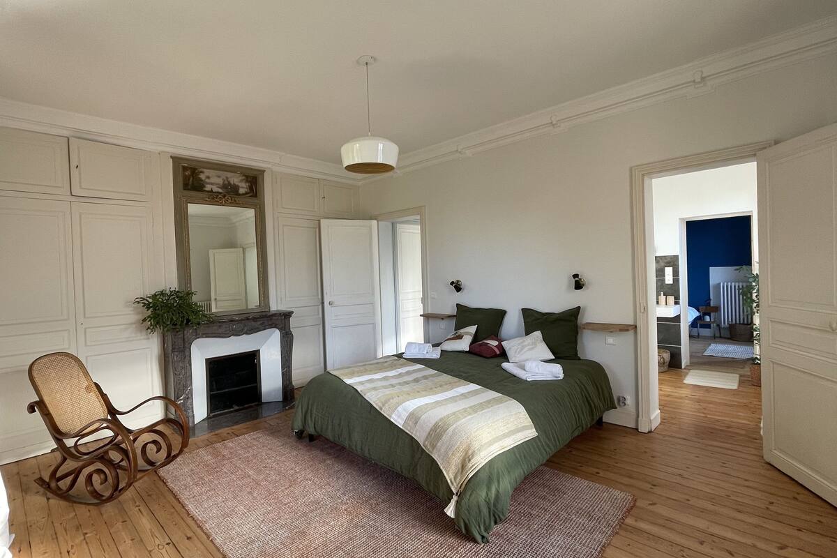 Quarto com cama, poltrona, lareira e espelho.