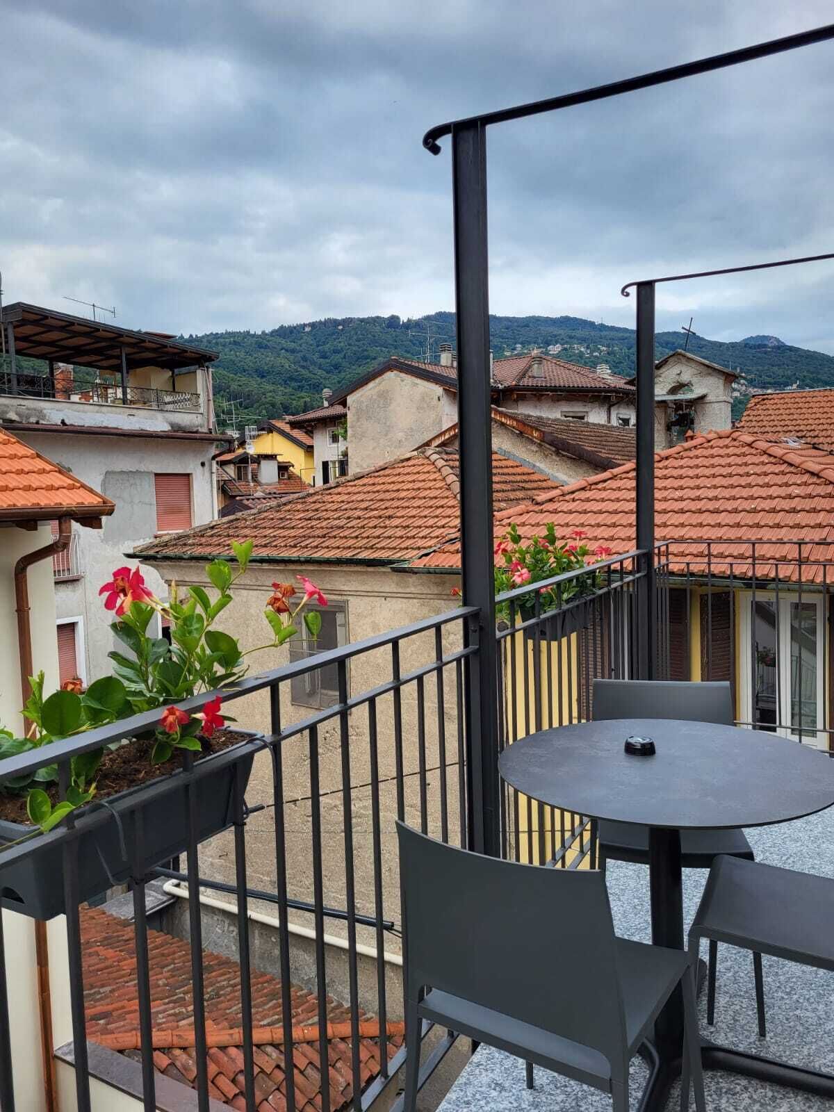 Uma varanda com uma mesa redonda e cadeiras, plantas em vasos e vista para edifícios com telhados de terracota ao fundo.