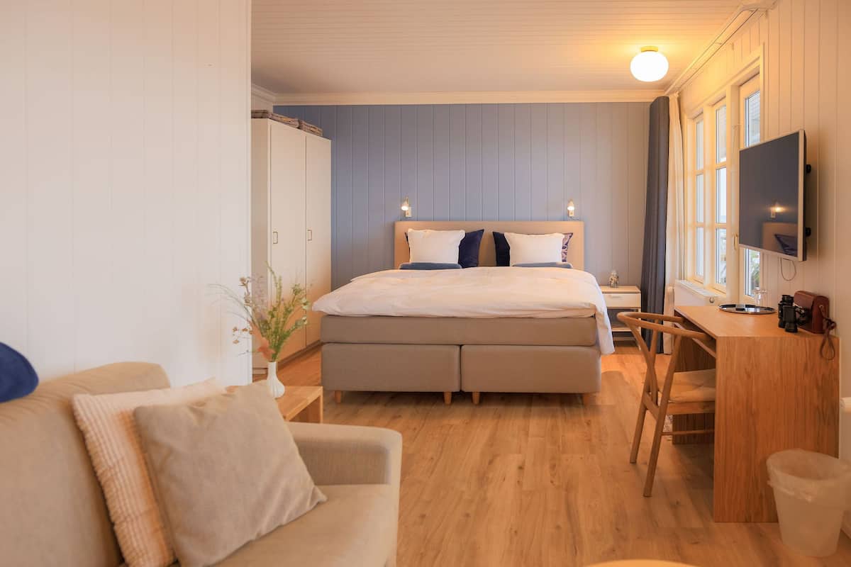 Um quarto com cama, mesas de cabeceira, escrivaninha, cadeira e televisão.
