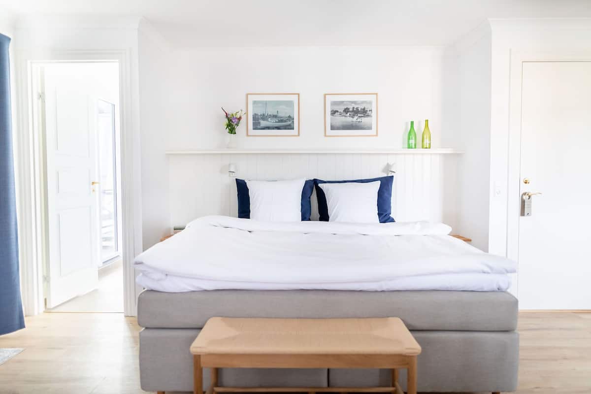 Quarto bem arrumado com cama, mesas de cabeceira e um banco.