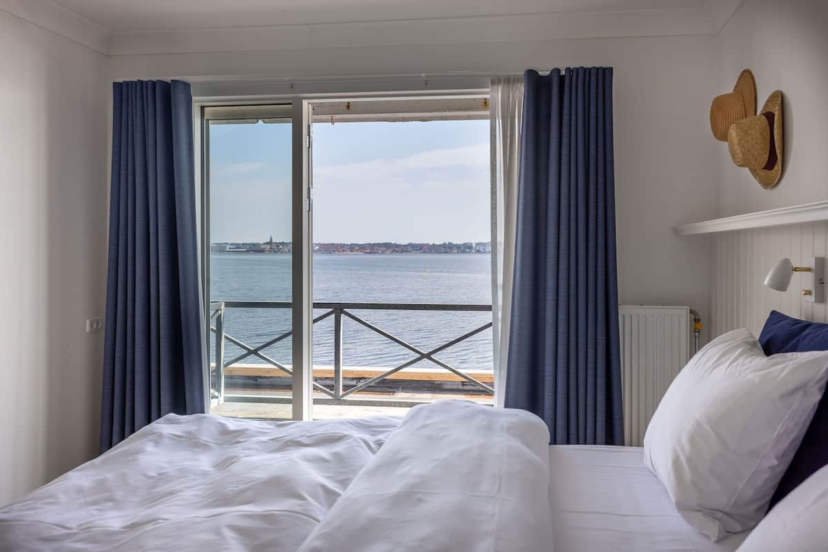 Um quarto com uma cama, vista para o mar e varanda.