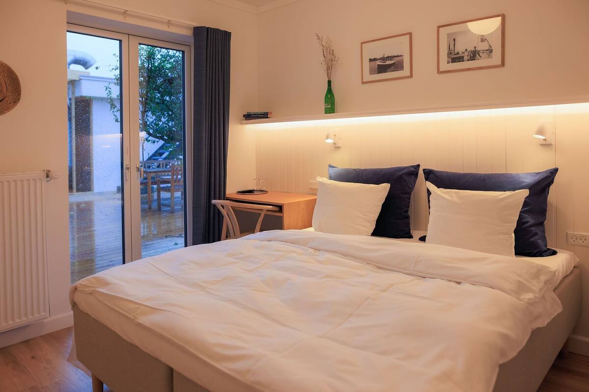 Quarto de hotel com cama, escrivaninha, cadeira e vista para o exterior.