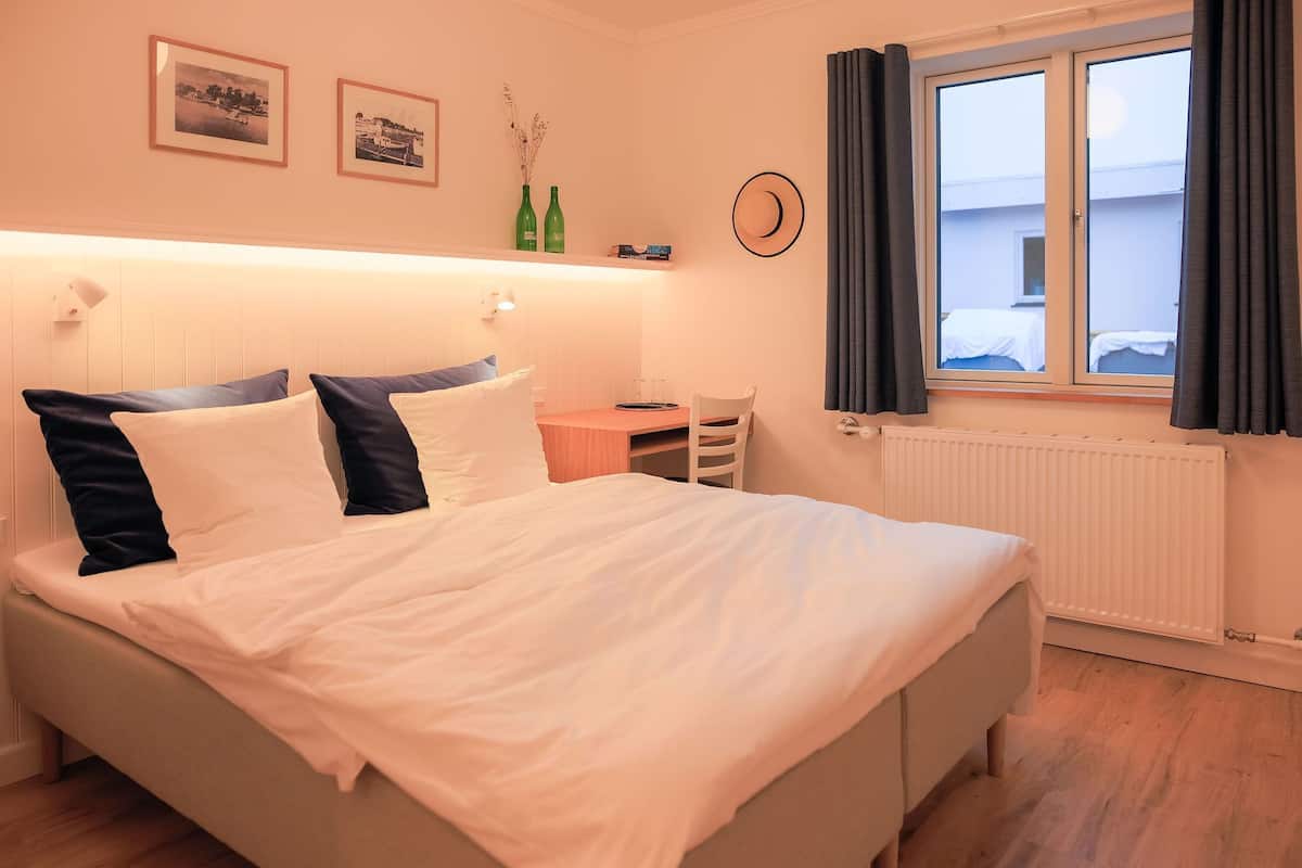Quarto com cama, escrivaninha, cadeira, janela com cortinas e radiador.