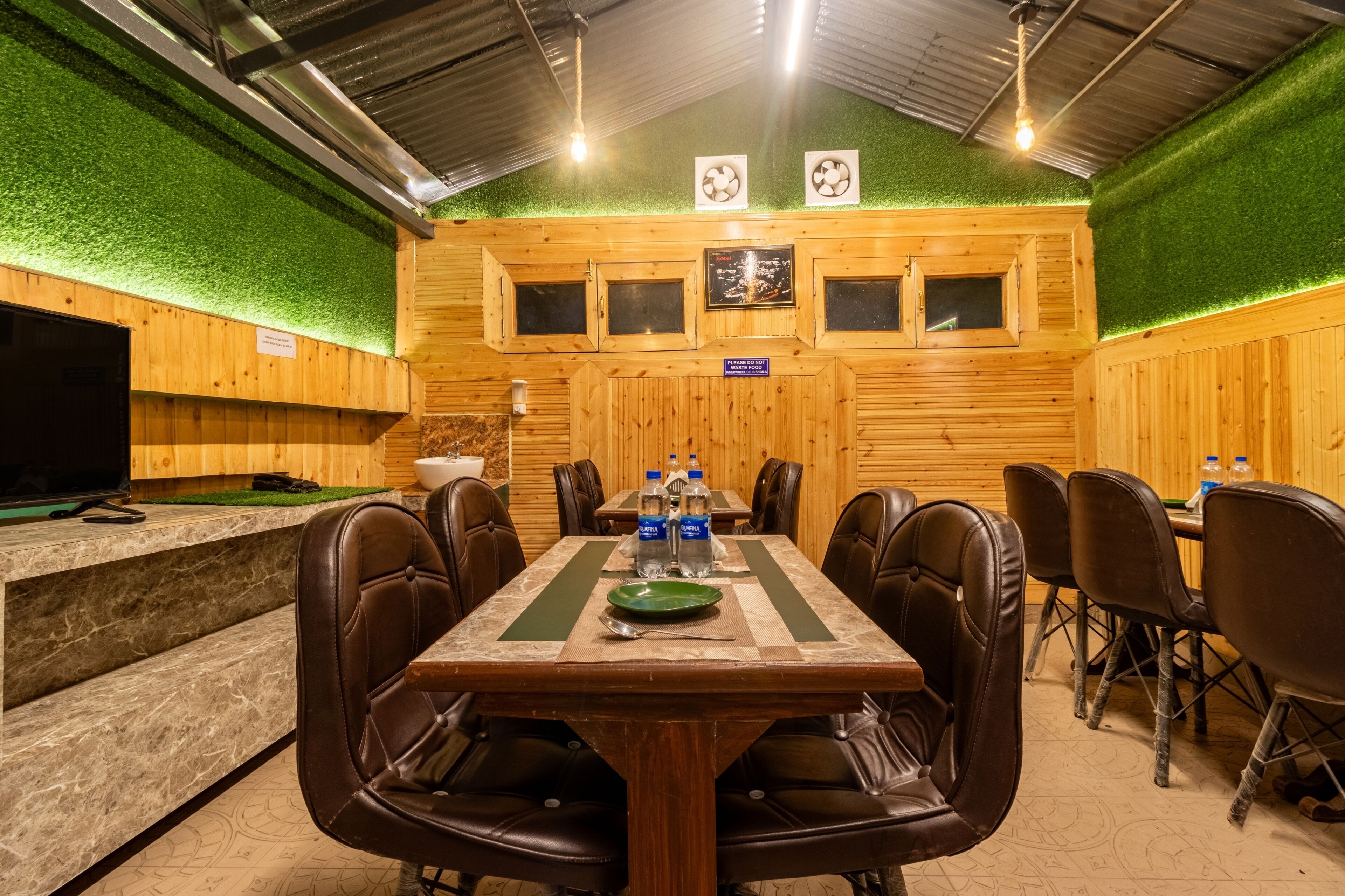 Sala de conferências com uma mesa e cadeiras de madeira, uma televisão e um aviso indicando área para fumantes.