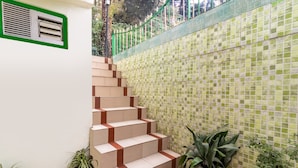 Uma escada com degraus bege e detalhes vermelhos, que leva a uma parede com azulejos verdes.
