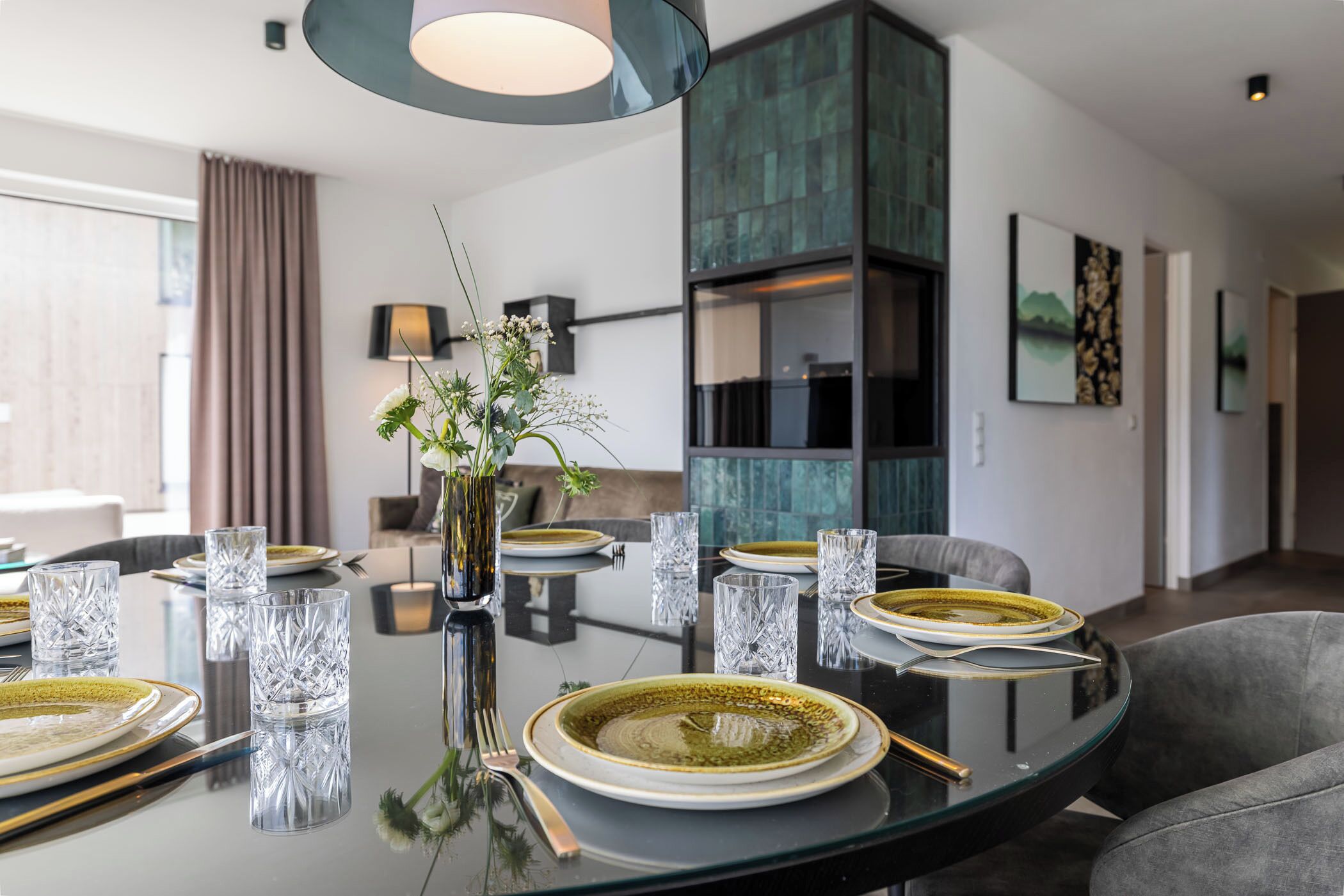 Uma sala de jantar com uma mesa redonda, copos de vidro transparentes e pratos postos para uma refeição.