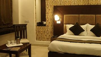 Quarto de hotel com uma cama grande, uma mesinha de cabeceira, uma cadeira, uma mesa com cafeteira e um ventilador de teto.