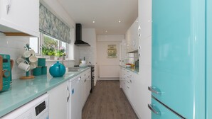 Uma cozinha moderna com armários brancos, uma geladeira verde-água e uma janela com vista para o verde.
