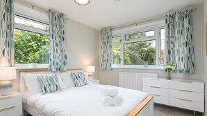 Quarto moderno com uma cama grande, mesas de cabeceira, cômoda e cortinas.