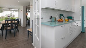 Cozinha moderna com armários brancos, bancada de vidro e área de refeições com cadeiras e mesa de madeira.