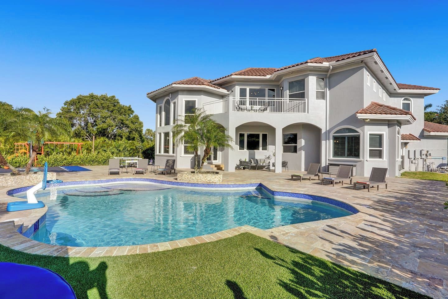 Uma casa de dois andares com piscina, móveis de jardim e um gramado bem cuidado.