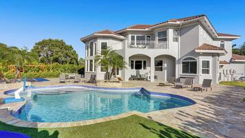 Uma casa de dois andares com piscina, móveis de jardim e um gramado bem cuidado.