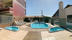 Área da piscina com duas piscinas pequenas, espreguiçadeiras e um edifício com fachada em azulejos.