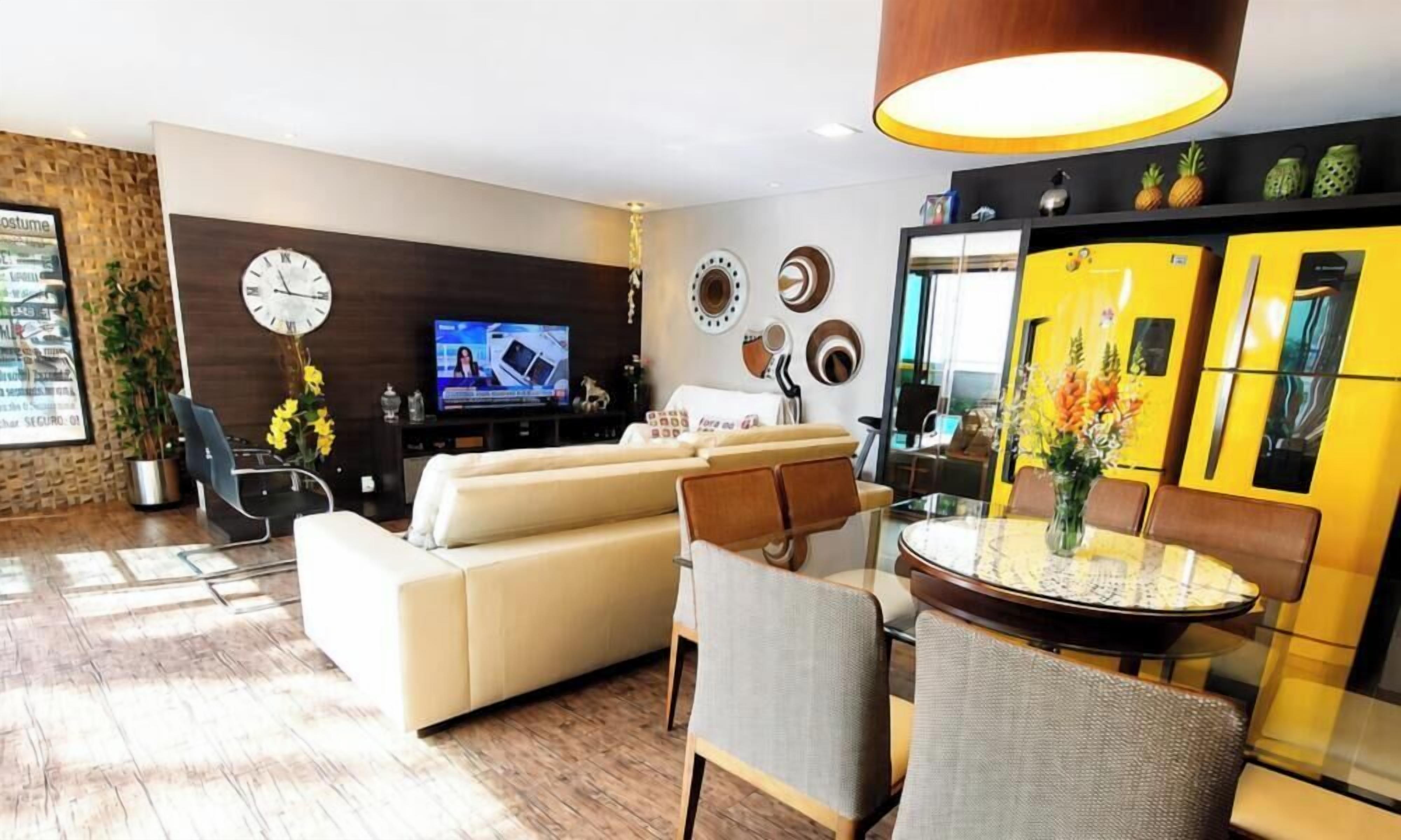 Uma sala de estar moderna com um sofá, cadeiras, televisão, pratos decorativos e uma geladeira amarela.