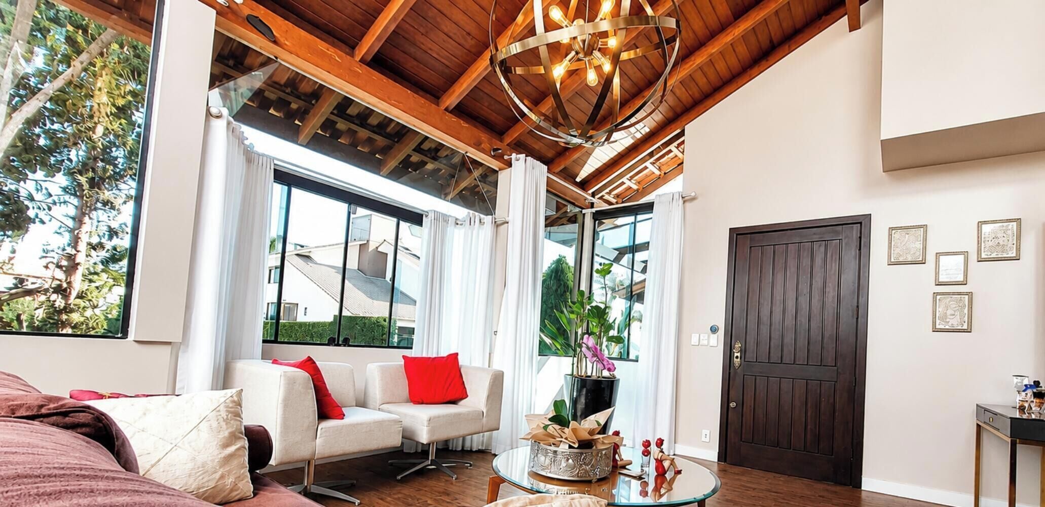 Uma sala de estar moderna com teto alto, grandes janelas, um sofá branco e uma porta de madeira escura.