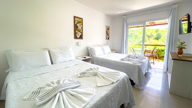 Quarto de hotel com duas camas, uma varanda com vista e uma pequena mesa com uma planta em vaso.