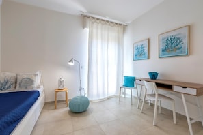 Quarto com cama, escrivaninha, cadeira, abajur e duas pinturas na parede.