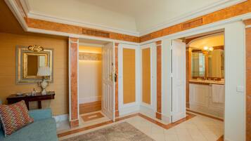 Quarto de hotel com sofá, espelho, porta para um banheiro e piso ladrilhado.