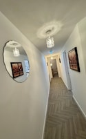 Um corredor com piso de madeira em padrão herringbone, um espelho oval grande e duas luminárias de cristal.