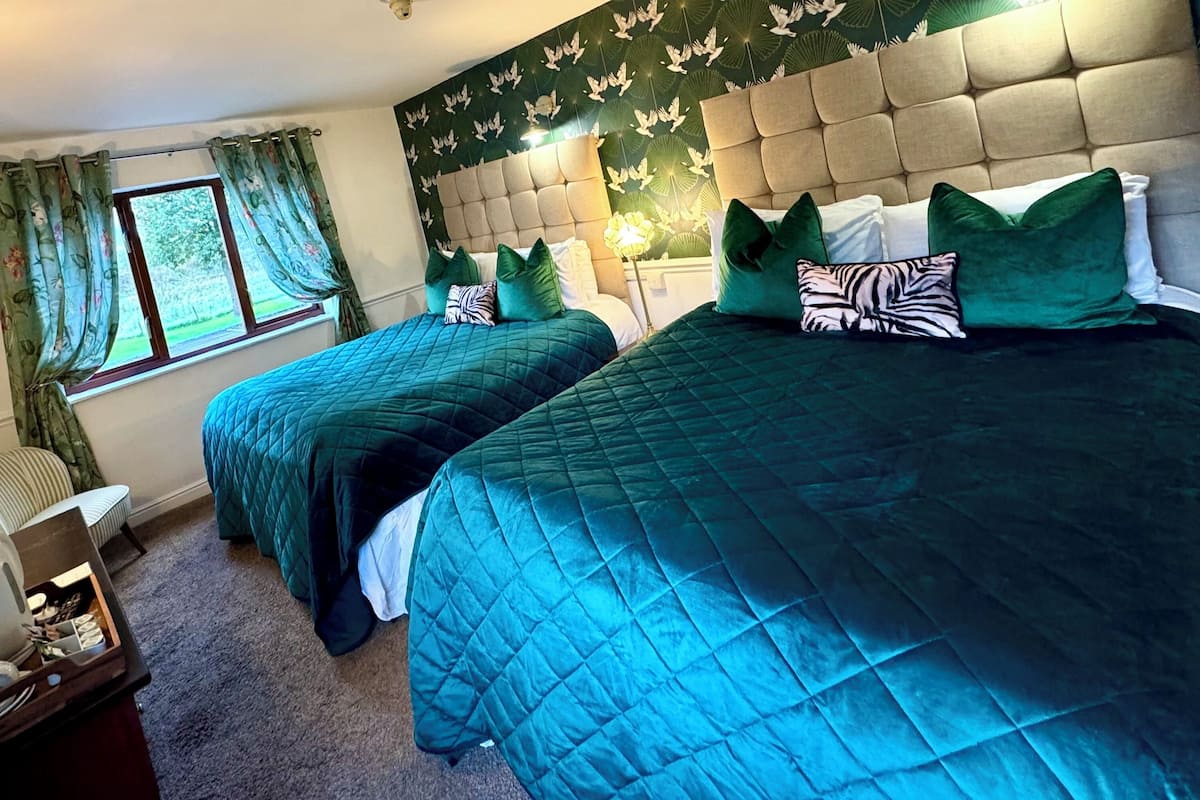 Quarto de hotel com duas camas, televisão, janela com cortinas e mesa de cabeceira com abajur.