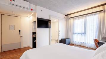 Quarto de hotel com cama, televisão, ar condicionado, janela com cortinas e porta.
