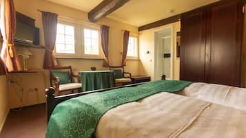 Quarto de hotel com cama, escrivaninha, cadeira, televisão e janela com cortinas.