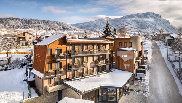 Um hotel com várias andares e varandas, paisagem coberta de neve e uma montanha ao fundo.