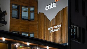 Um edifício moderno com um letreiro de 'cota' em destaque e o slogan 'equilíbrio entre trabalho e natureza'.