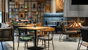 Um restaurante moderno com mesas e cadeiras de madeira, um espaço de estar acolhedor com assentos estofados em azul e uma lareira.