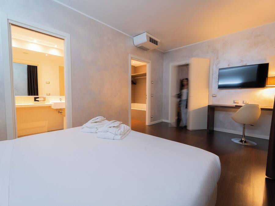 Quarto de hotel com uma cama grande, televisão na parede, escrivaninha com cadeira e um closet espaçoso.