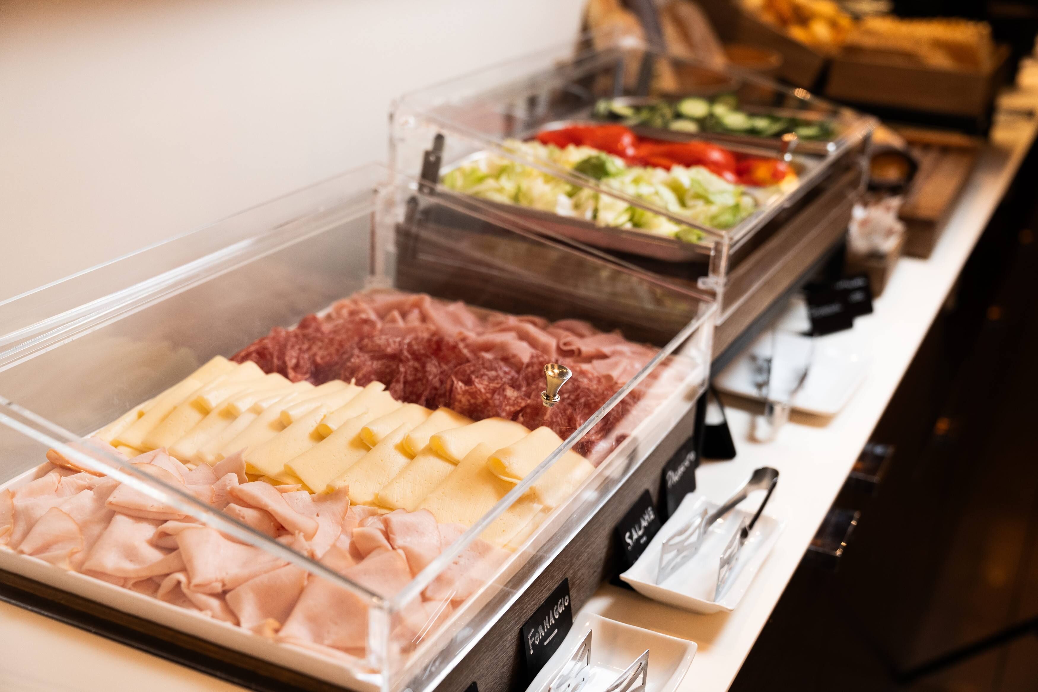 Buffet com diversas opções de comida, incluindo carnes, queijos e saladas.