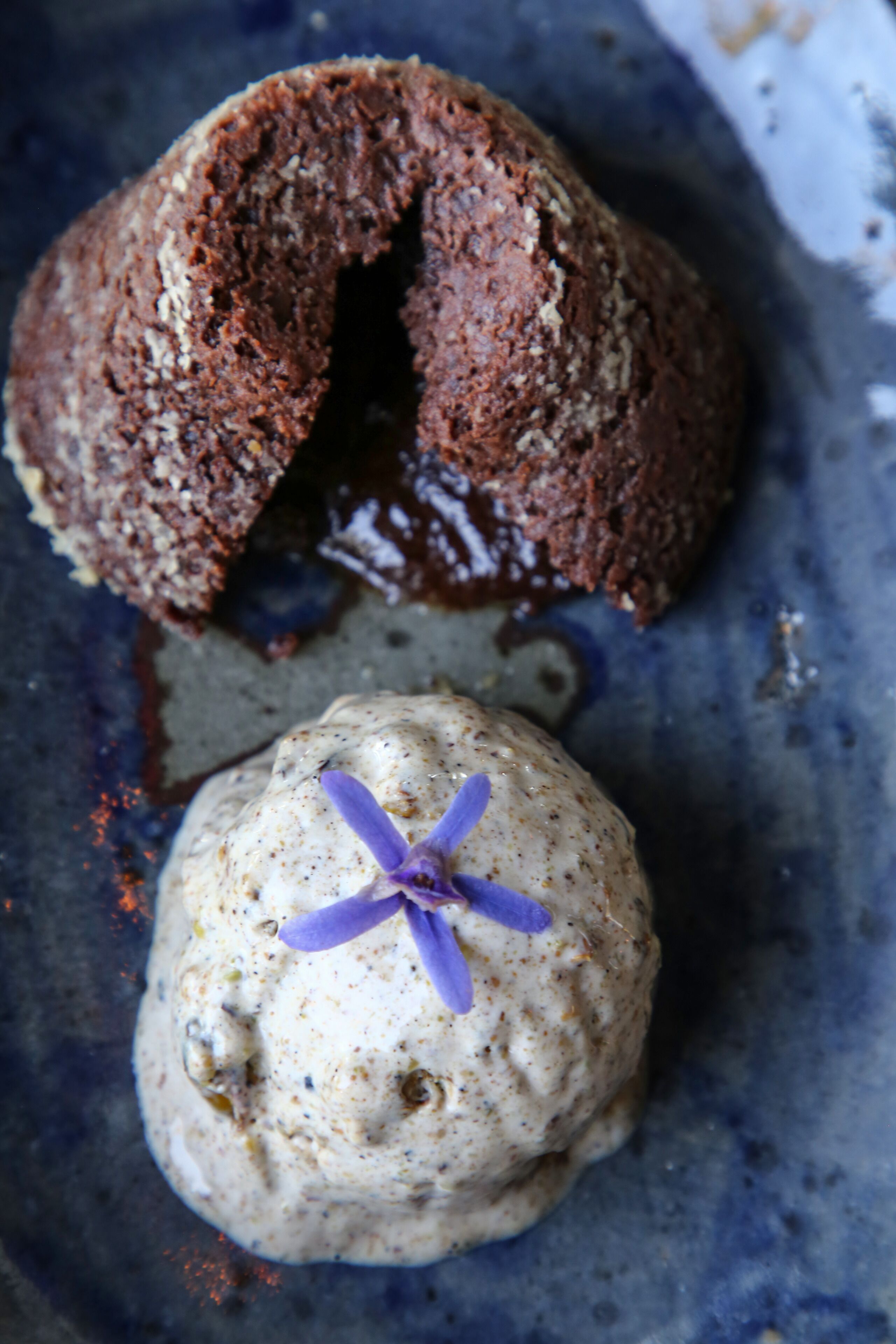 Sobremesa com bolo de chocolate e uma bola de sorvete com uma flor roxa em um prato.