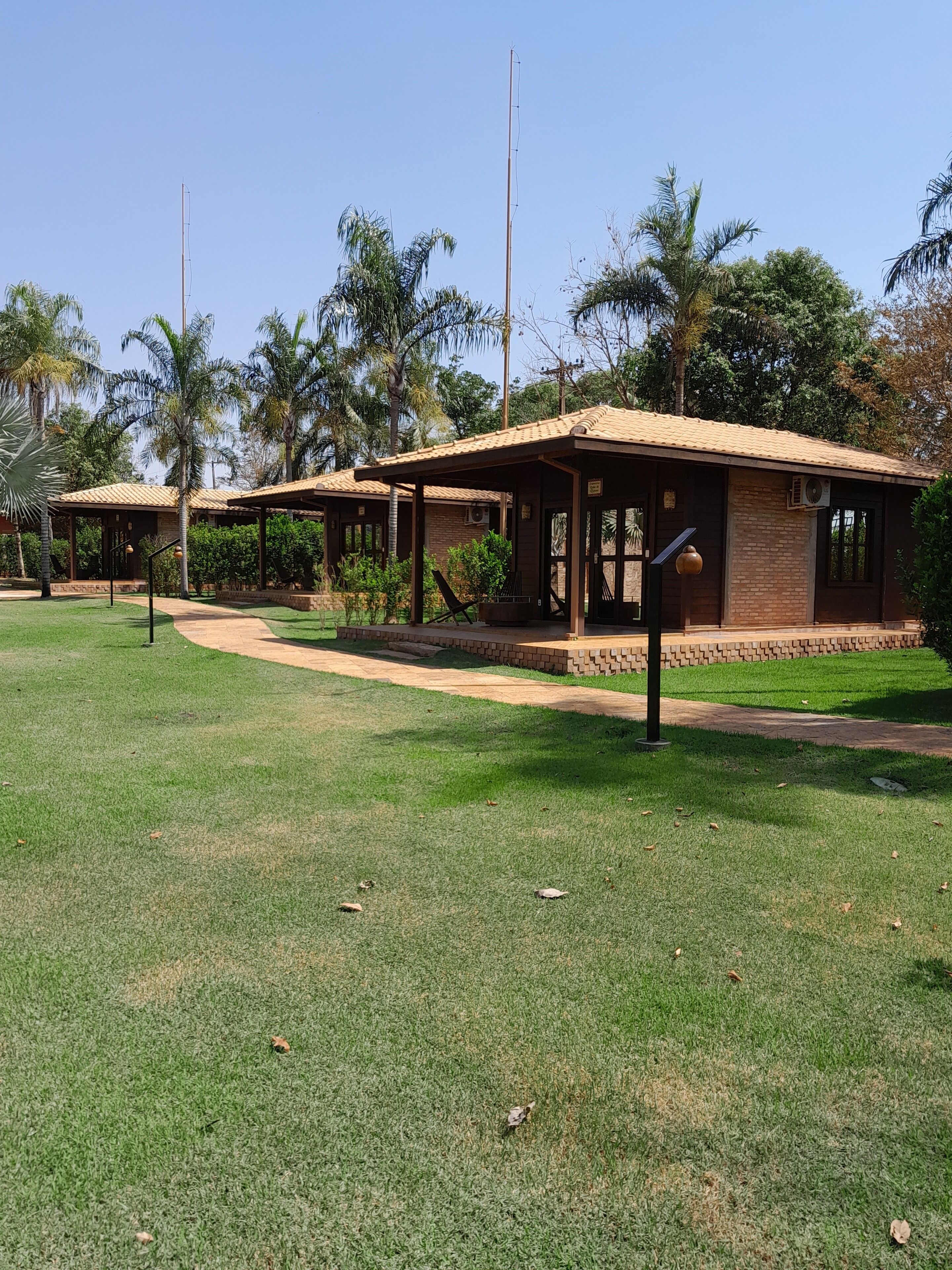 Conjunto de pequenos edifícios térreos com telhados de cerâmica, rodeados por grama bem cuidada e palmeiras.